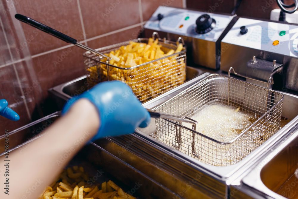 Foto de French fries cooking. Grid with strips hop potato lowered into ...