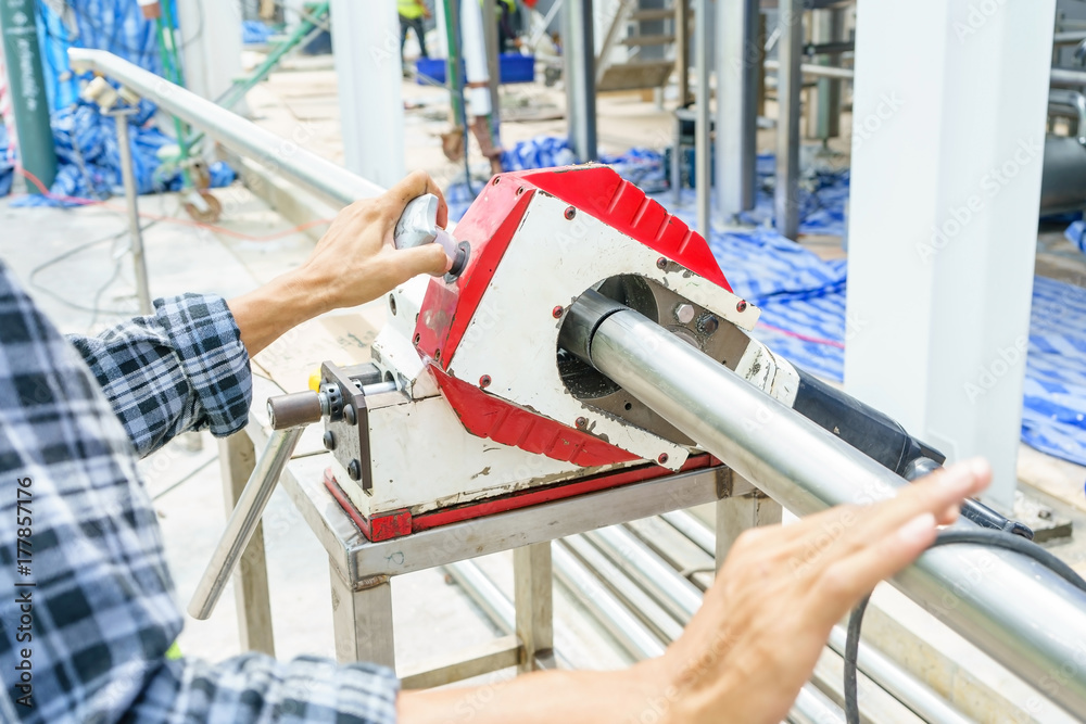 Construction Worker sawing a pipe by portable orbital pipe cold cutting ...