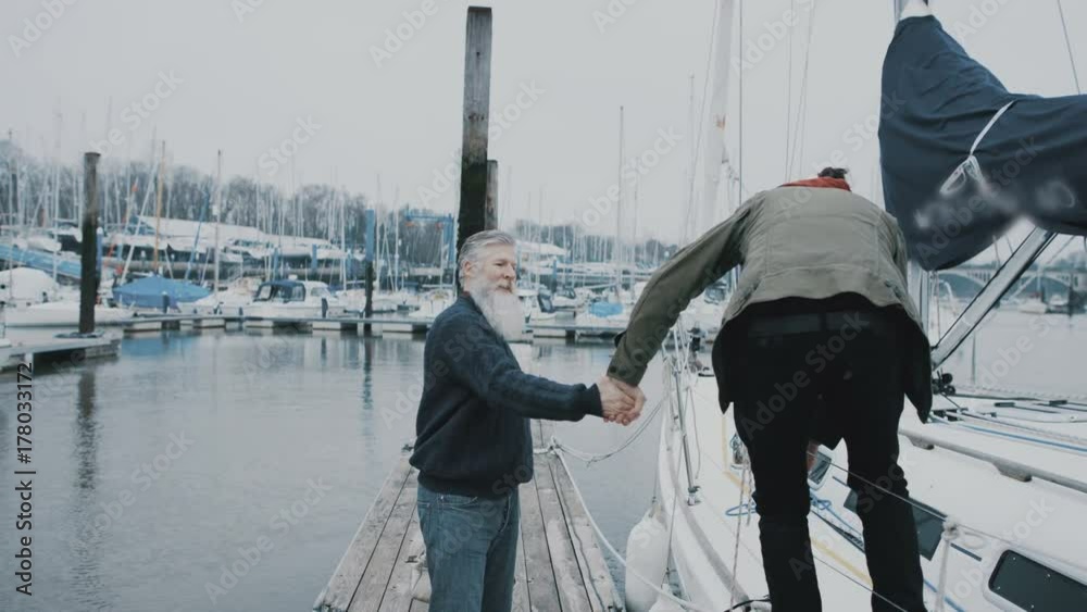 Father & son getting off of boat & walking along the jetty in a marina ...