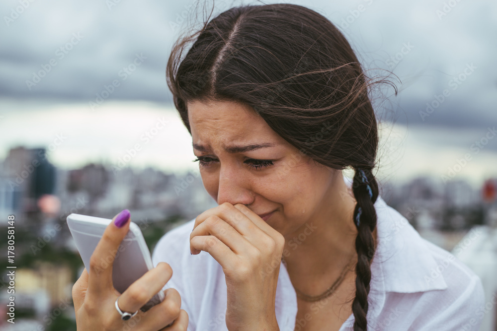Woman looking at her phone and crying Photos | Adobe Stock