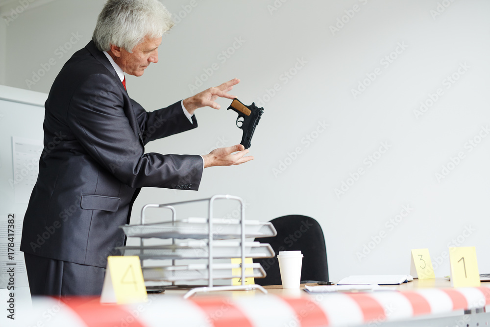 Senior crime scene investigator in classical suit holding gun at hands ...