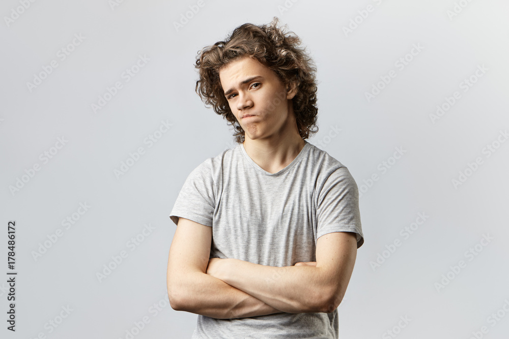 Studio shot of handsome suspicious young man keeping arms crossed, his ...