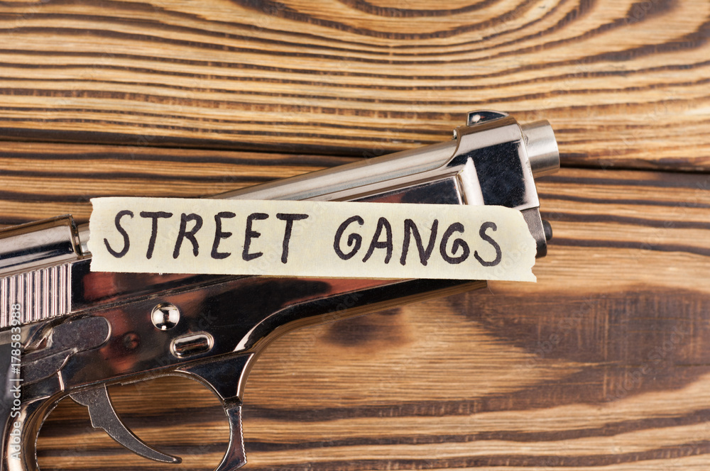 Inscription STREET GANGS on torn paper and glossy pistol on old rustic ...