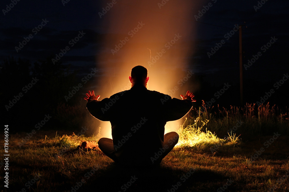 A bearded man sits by the fire holding out his hands to the fire. The ...