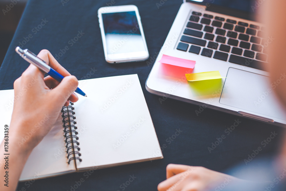 Woman hand works in a laptop computer and is writing on notepad with a ...