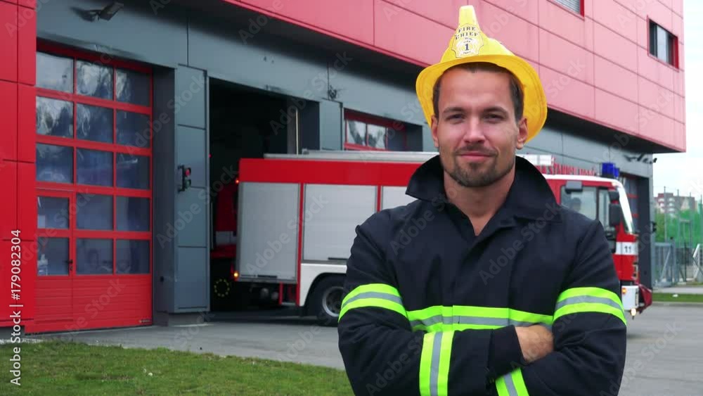 A young firefighter looks at the camera with arms folded across chest ...