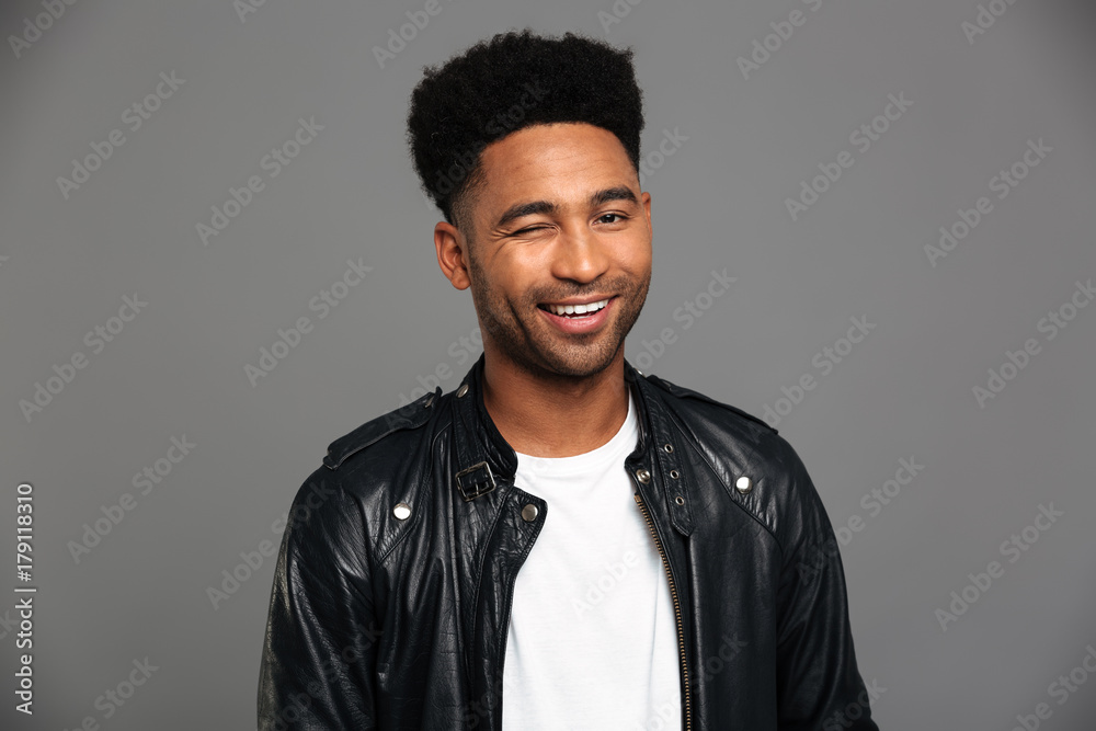 Young smiling african man in black leather jacket winks one eye ...
