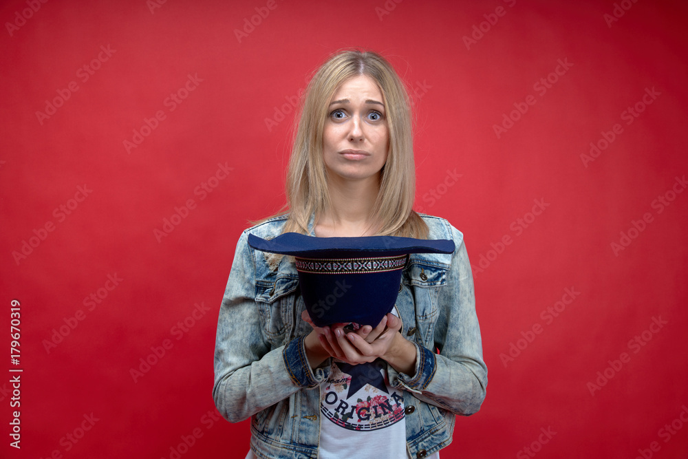 young blonde woman in denim jacket holds his hat in hands in front with ...
