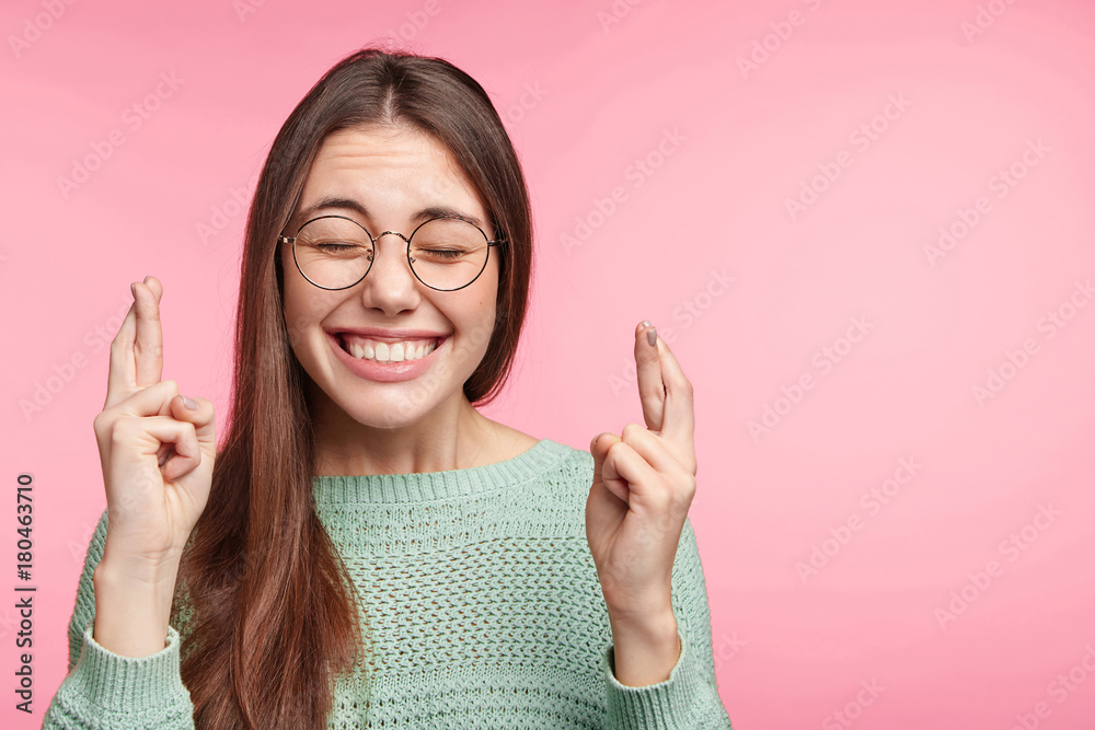 Glad positive female model dressed casually, keeps fingers crossed ...