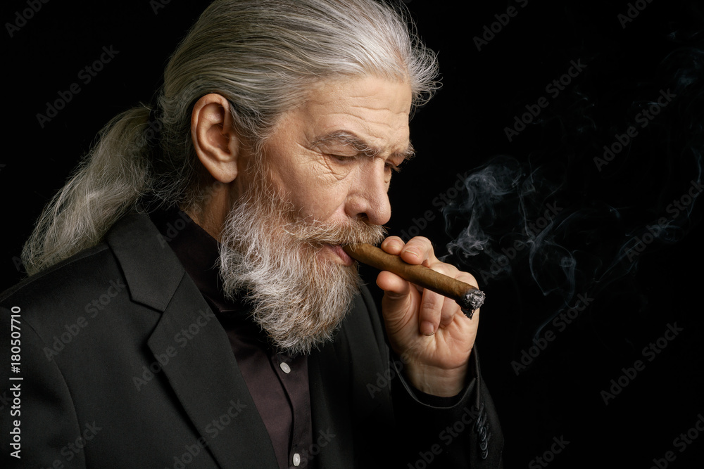 Side view of wrinkled stylish man with a cigar. Portrait of aged grey haired man smoking cigar ...