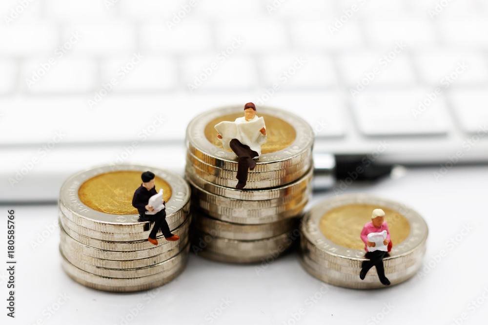 Miniature people reading and sitting on coins stack with keyboard ...