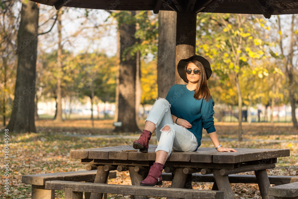 Beautiful teenage girl sitting on the park bench with black hat blue ...
