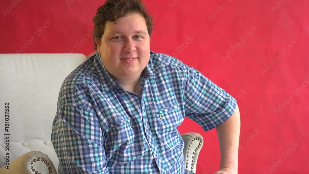 Fat man sitting in armchair and is looking at camera against red ...