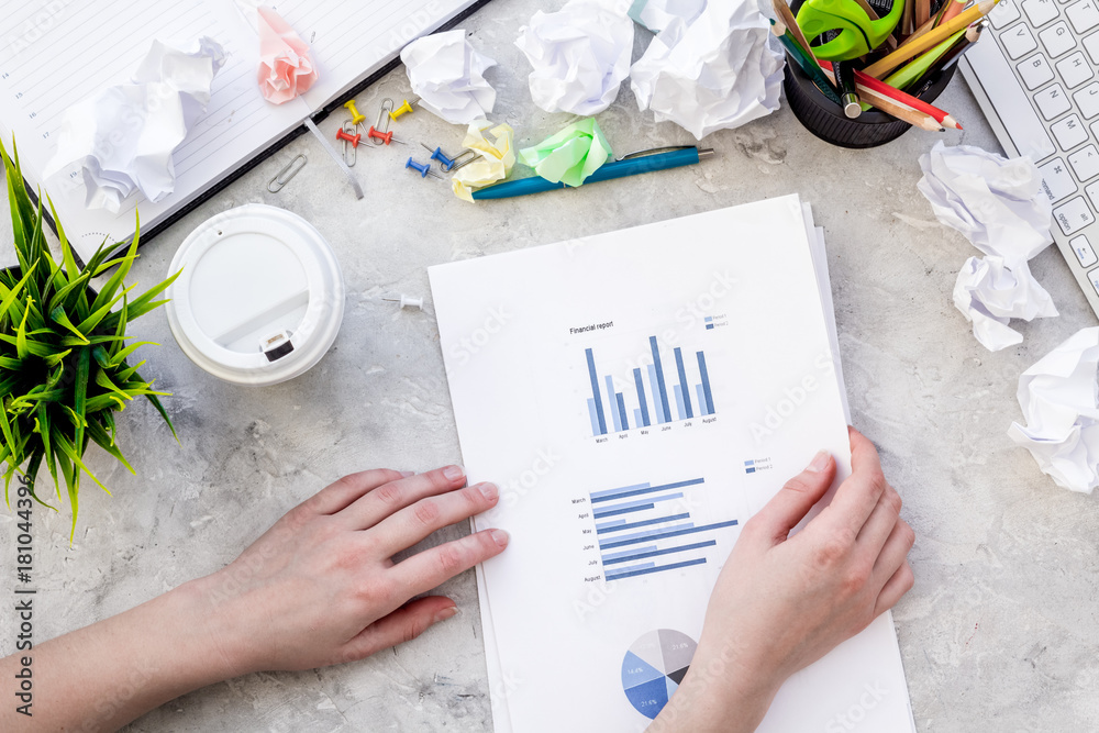 Chaos in office.Desk covered with crumpled paper and scattered stationery. Hands hold sheet with ...