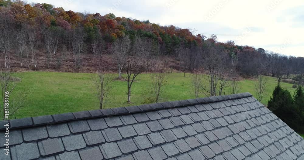 A slow reverse aerial view revealing a farmhouse's roof and shingles ...