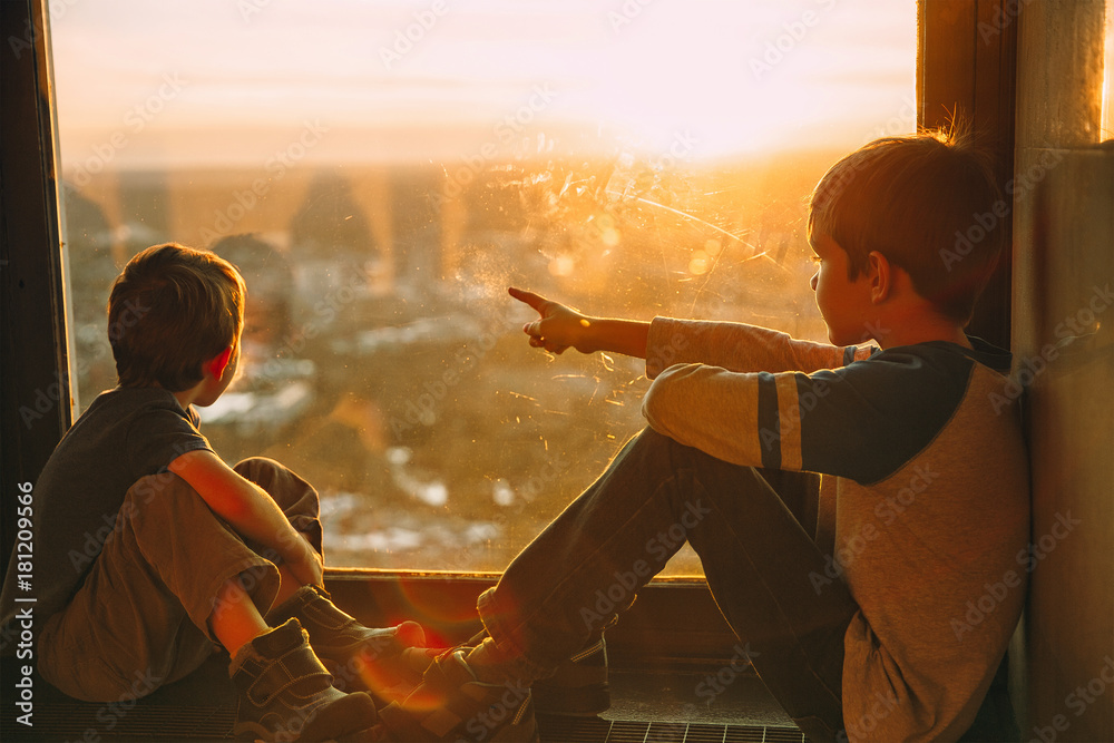 children sitting on the windowsill. Two boys looking out the window at ...