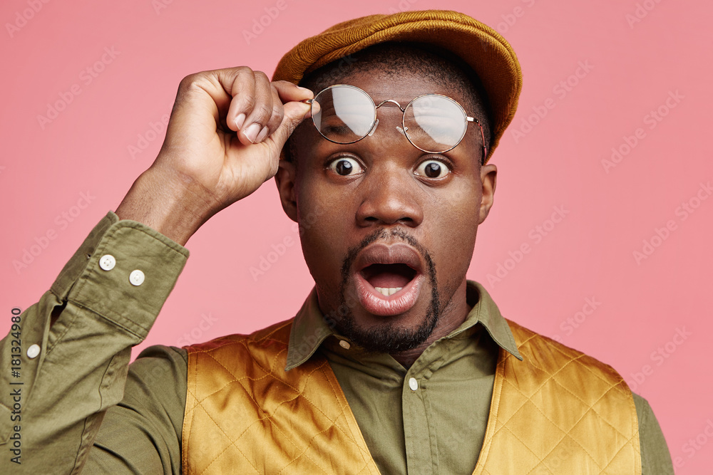 Stupefied black male model takes off glasses, stares at camera, has ...