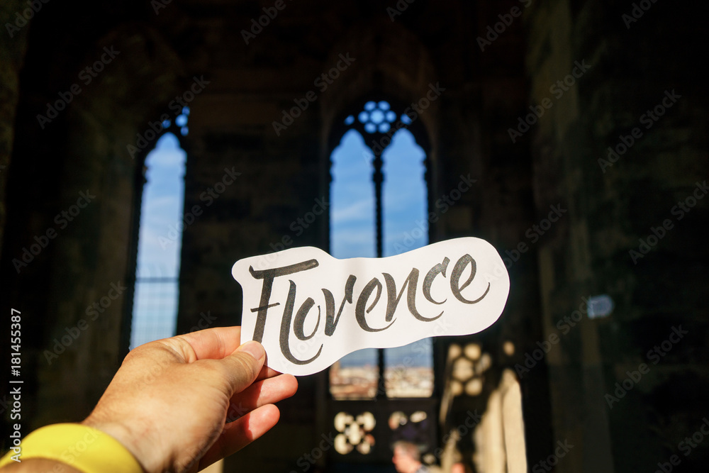 Hand written lettering card in men's hand with word Florence in front of typical Florence window ...