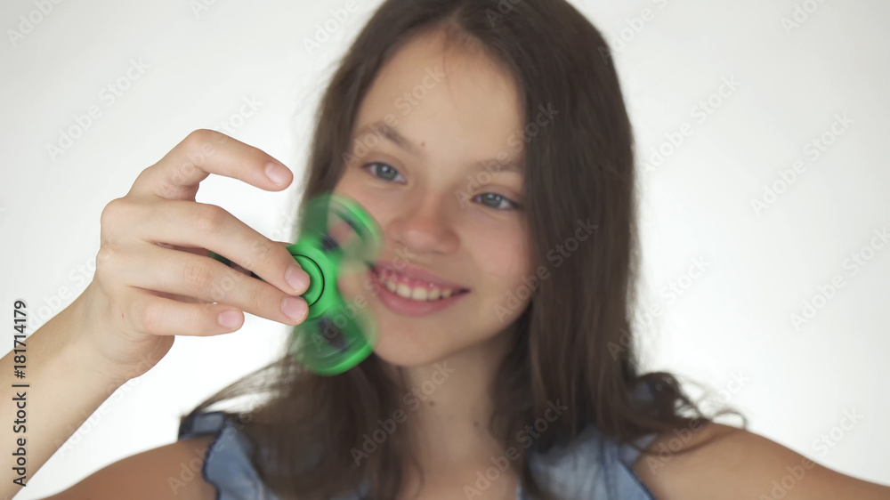 Beautiful cheerful teen girl playing with green fidget spinner on white ...