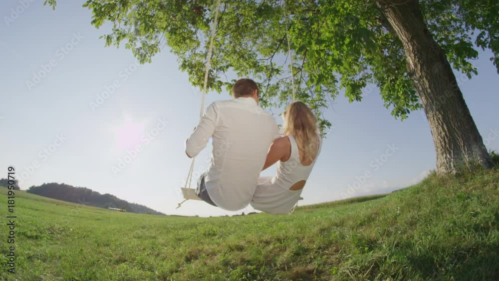 SLOW MOTION: Cheerful young couple swinging on swing under green tree ...