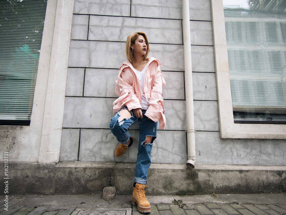 Fashionable Chinese girl in pink coat and ripped jeans standing in ...