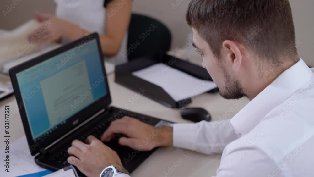 The young man prints the text on the laptop, the person looks at the ...