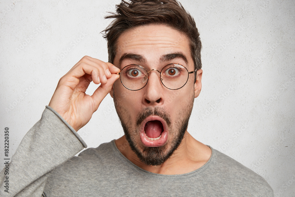 Close up shot of shocked stunned male stares at camera with jaw dropped ...