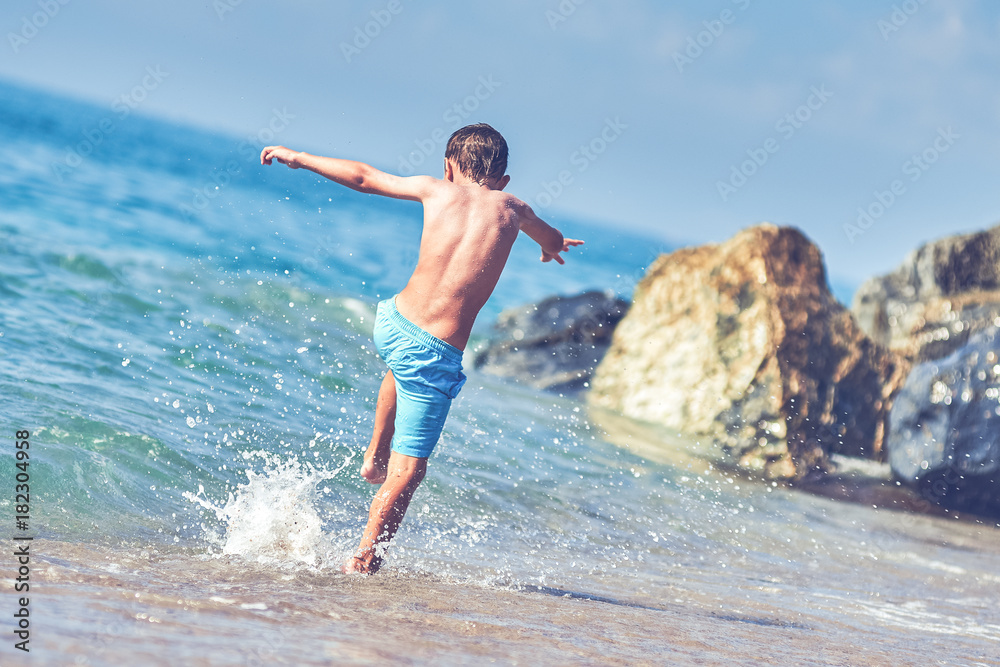 Cute Caucasian boy is running in the water along the sea shore. Back ...
