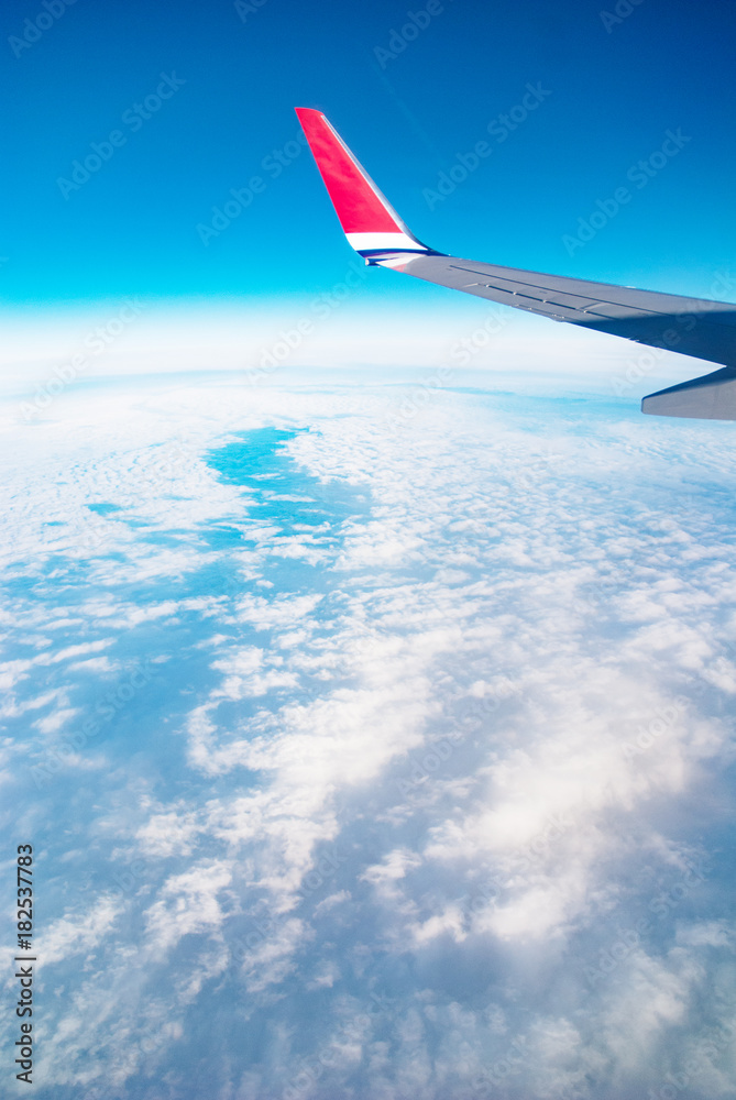 Airplane window view with a wing and curved Earth below, bright sky ...