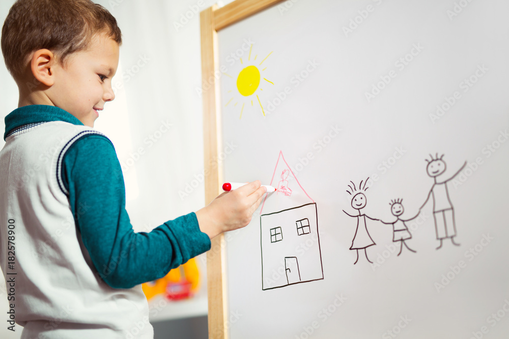 Cute little boy drawing on white board with felt pen and smiling. Early ...