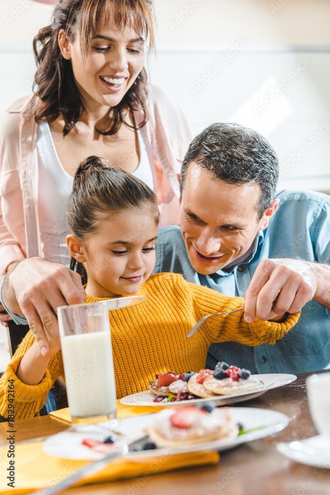 cheerful family together eating pancakes with berries at table on ...