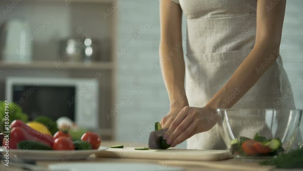 Woman cutting cucumber while making salad in her kitchen at home ...