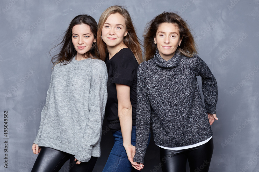 Three different attractive women posing in front of grey studio wall ...