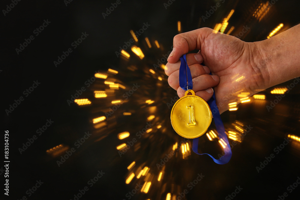 Man hand holding gold medal against black background with glitter ...