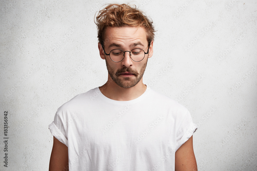 Curious intelligent male wears round spectacles, casual t shirt ...