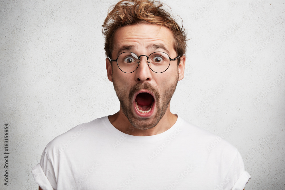 Emotional bugged eyed stylish man keeps mouth widely opened being ...