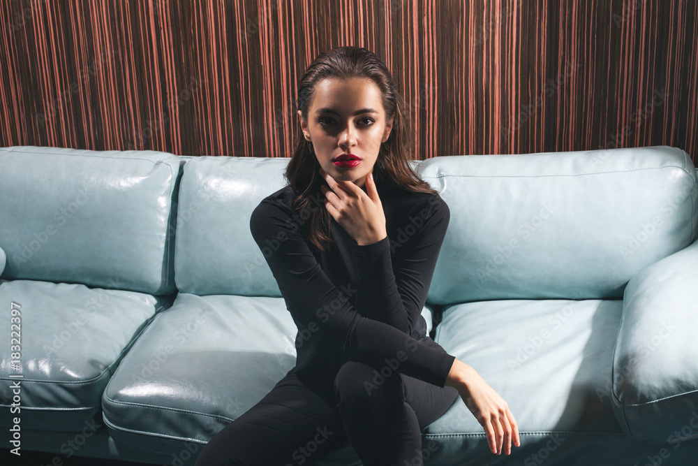 stylish caucasian woman in strict black clothes sitting on leather sofa ...