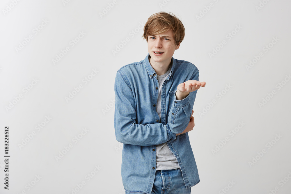 Confused angry fair-haired young male student gestures in bewilderment ...