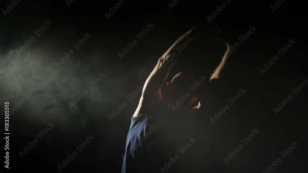 Silhouette of a man stretching in a darkened room with a single ray of ...