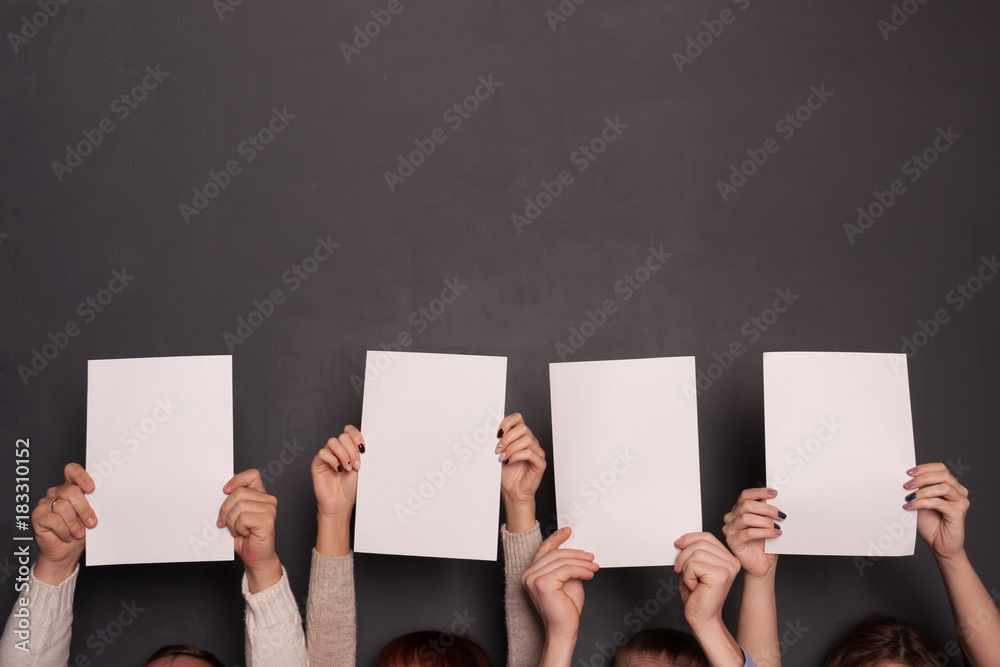 Group of four people holding paper sheets above heads on gray ...