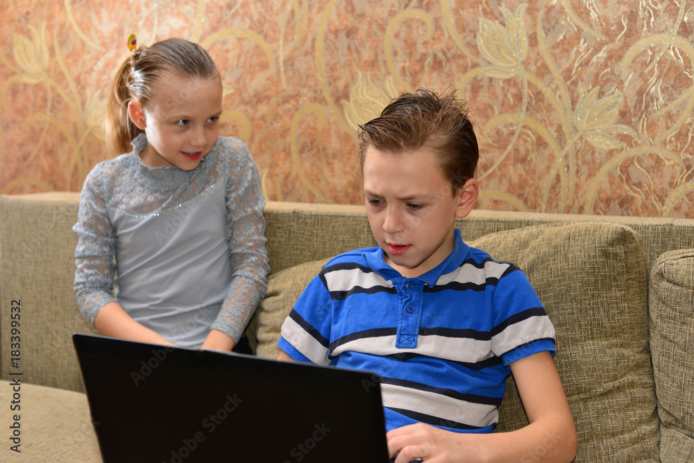 Brothers and sisters use tablet PC and laptop. Boy and girl sitting on ...
