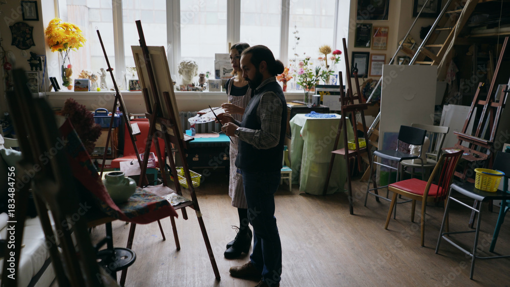 Skilled artist man teaching young girl to draw paintings and explaining ...
