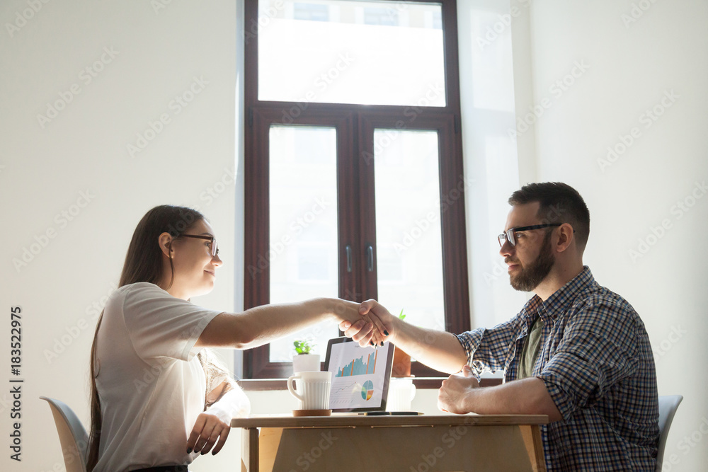Friendly millennial businessman and businesswoman handshaking over ...