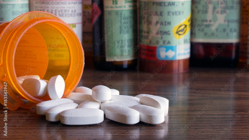 Prescription opioids with many bottles of pills in the background ...