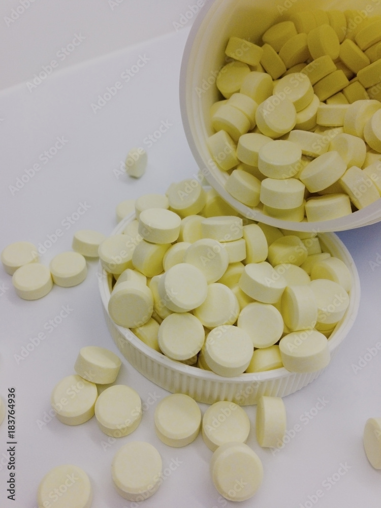 Milk tablets are being poured out of a white plastic bottle into the ...