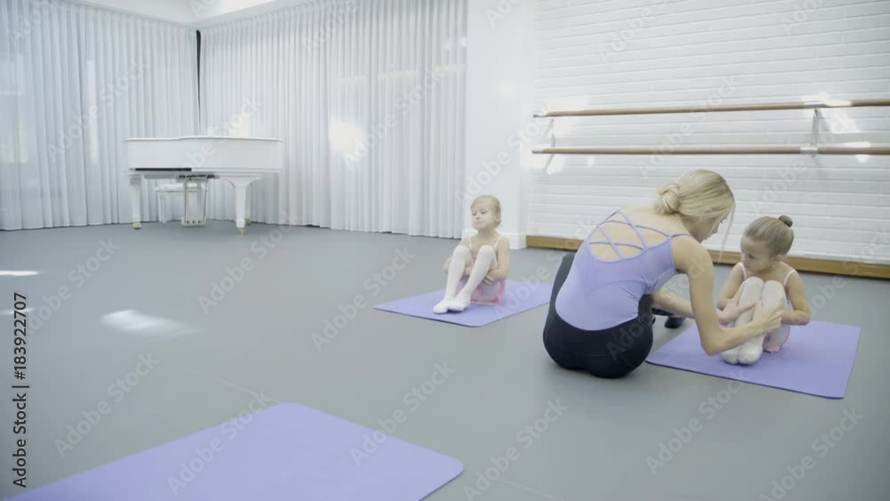 In dance studio coach corrects position of little girls sitting. In ...