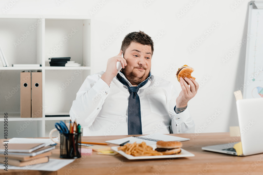 overweight businessman talking on smartphone while eating fast food in ...