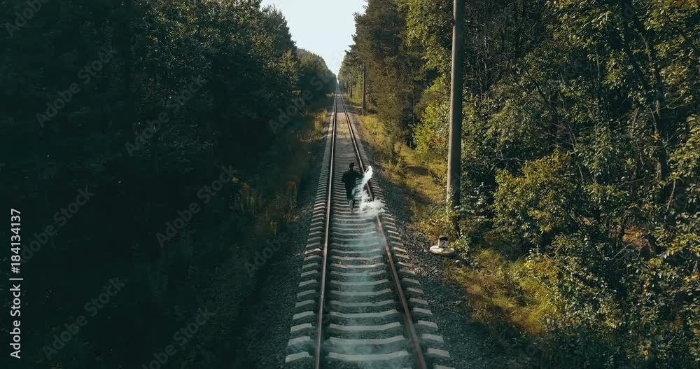 Man running on train tracks with smoke bomb. Drone back view. Runner ...