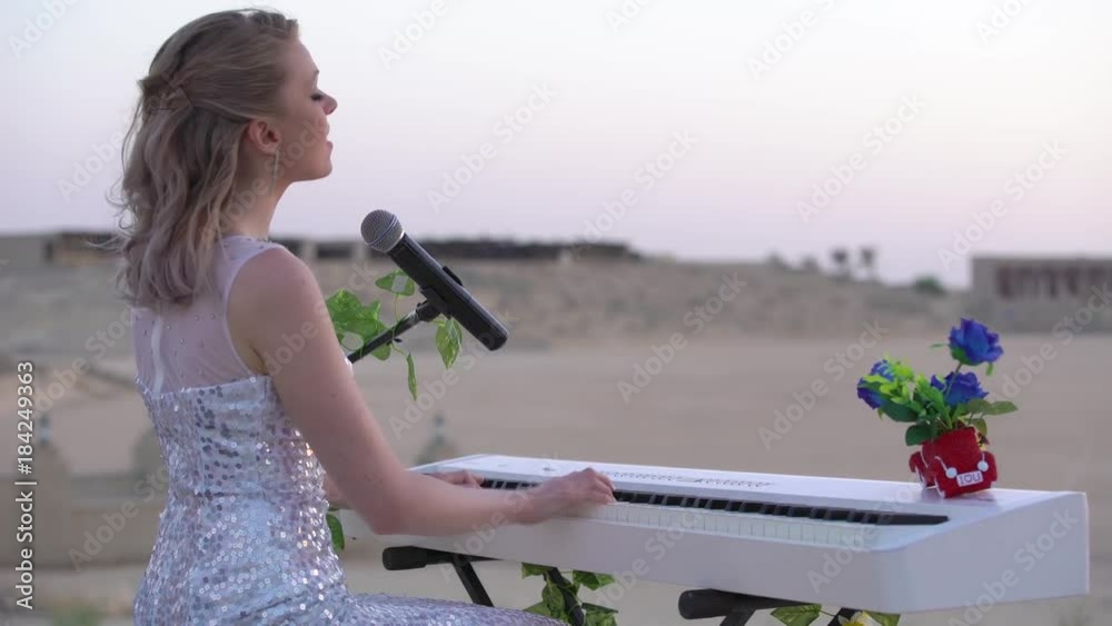Elegant young blonde woman sings, plays romantic music on white digital ...