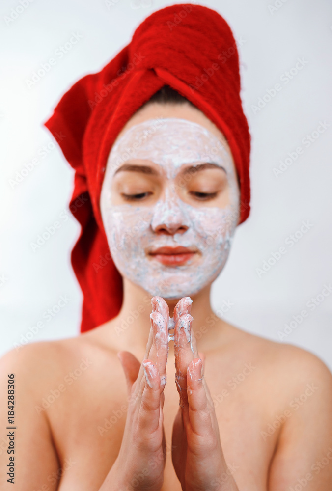 beautiful girl with a red towel on her head applies a scrub on the face ...